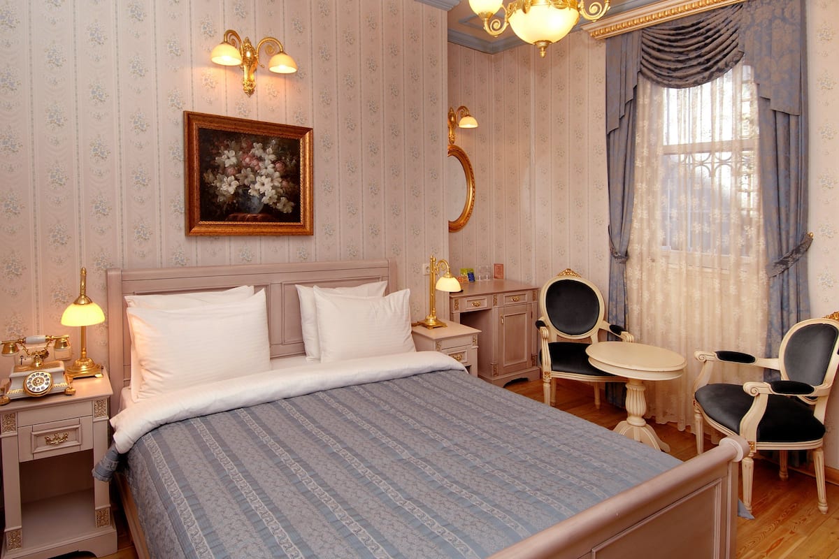 Quarto de hotel clássico com uma cama grande, uma escrivaninha, duas cadeiras, um espelho e um candelabro.