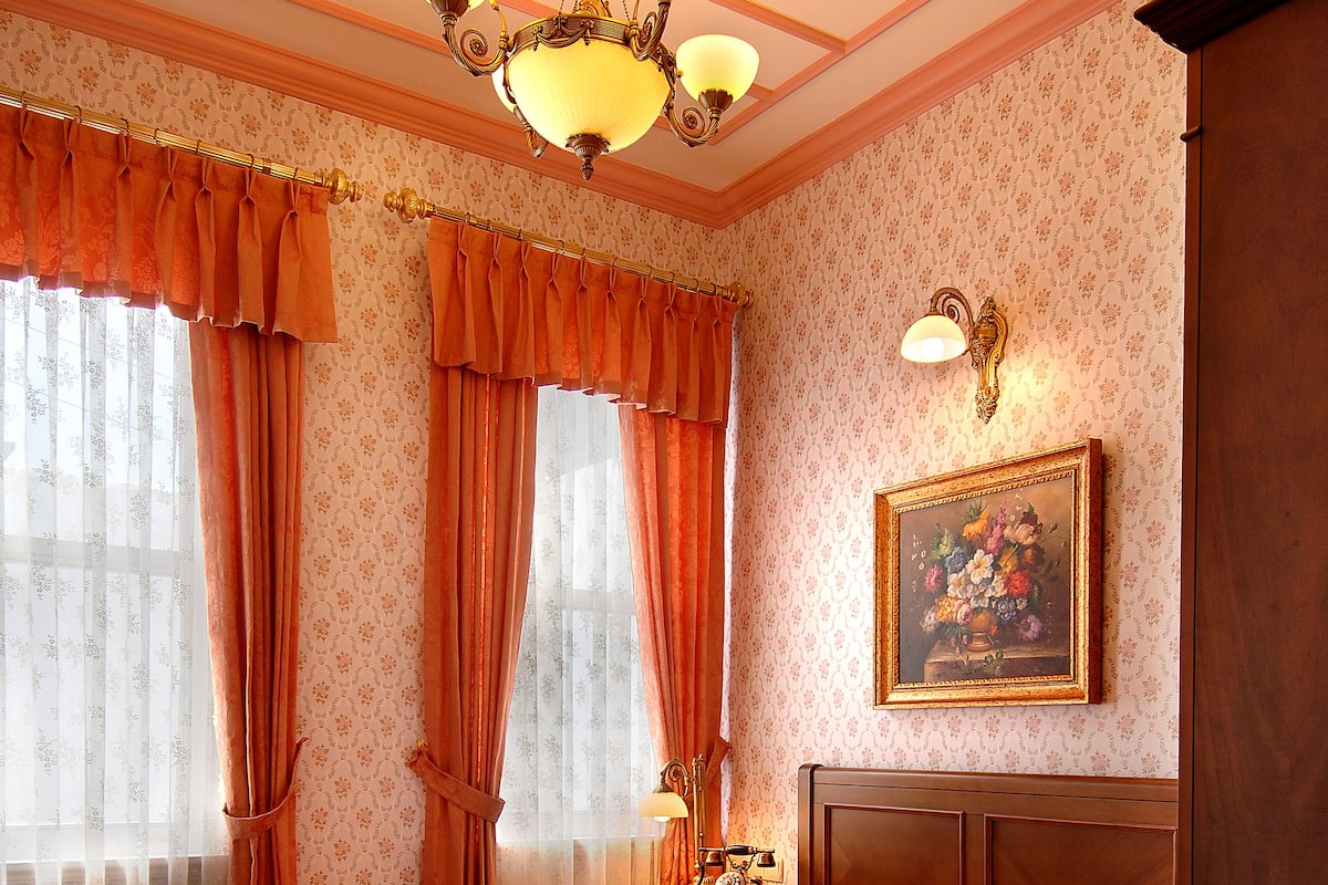 Quarto com cama de madeira, um lustre e papel de parede estampado com motivos florais.