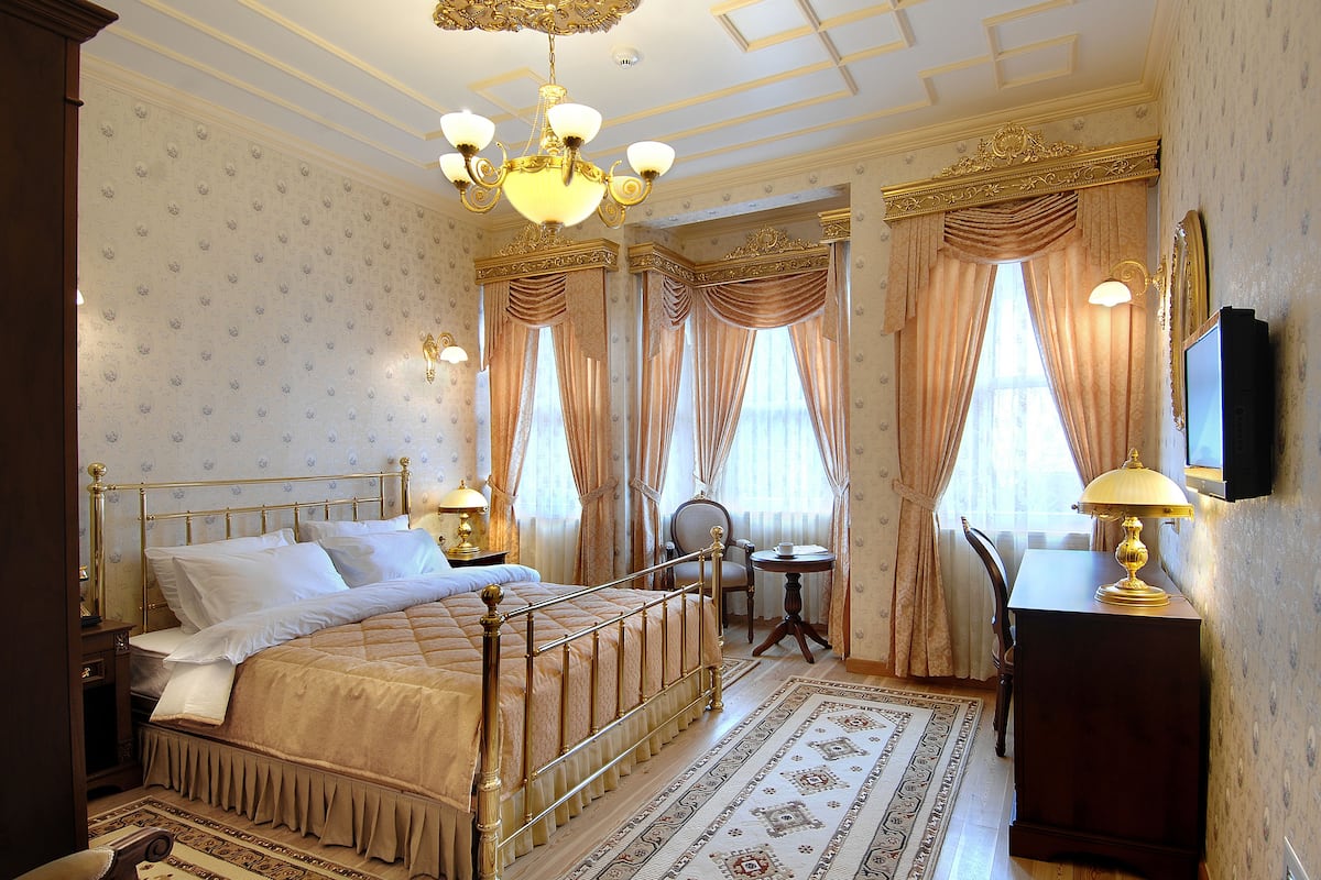 Um quarto clássico com cama de dossel, um candelabro, uma escrivaninha com abajur e uma televisão na parede.