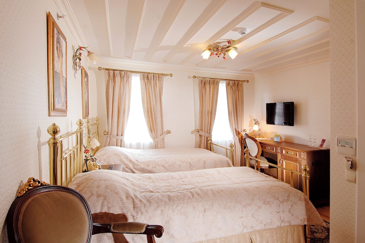 Quarto de hotel com duas camas, cómoda de madeira, televisão e candelabro.