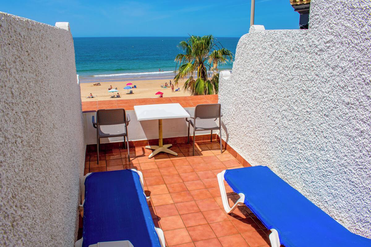 Terraço com vista para a praia, duas cadeiras de descanso azuis, uma mesa e uma decoração com tema de estrela-do-mar.