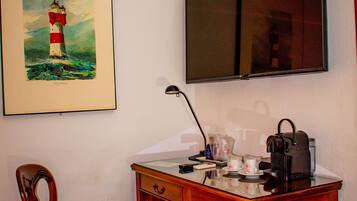 Um quarto com uma escrivaninha de madeira, uma cadeira, um quadro de um farol, uma televisão montada e um aparelho de ar condicionado.