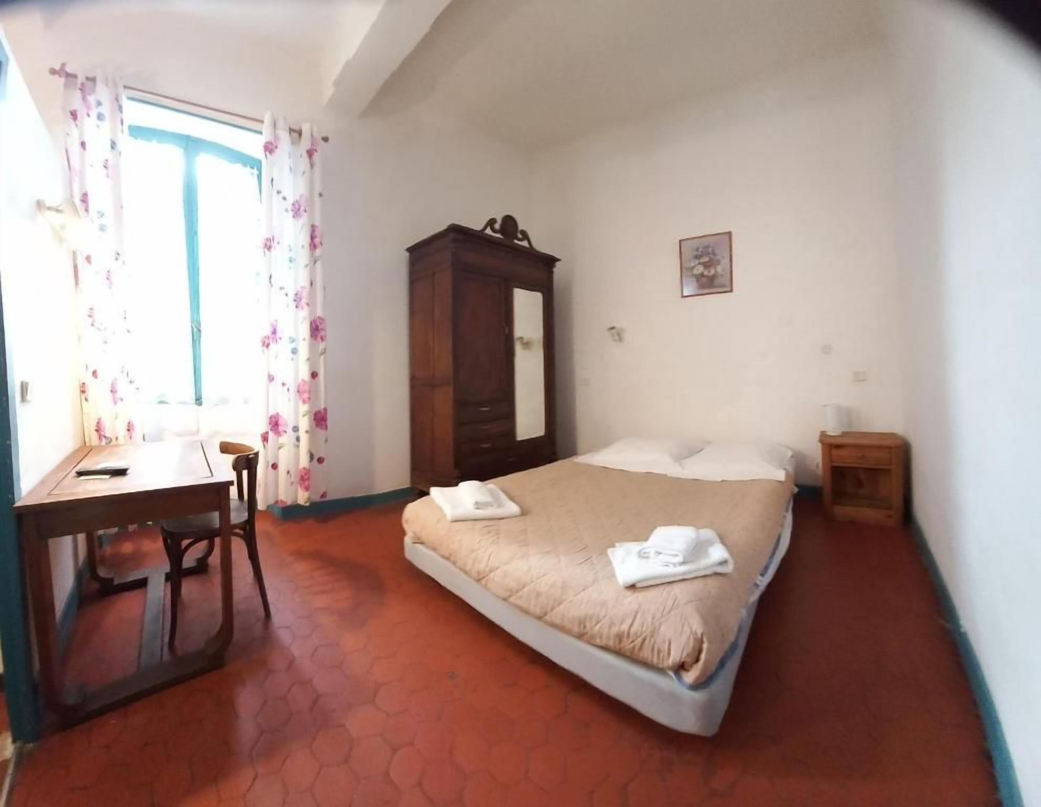 Quarto com cama, guarda-roupa de madeira, escrivaninha e cadeira.