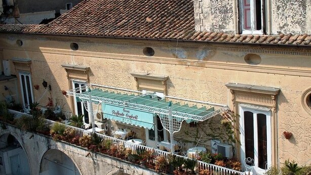 Edifício com marquise verde e área externa com mesas e plantas.