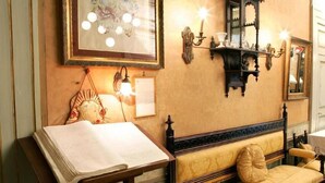 Quarto antigo com uma cama, um sofá, uma mesa com um livro, arandelas de parede e um espelho.