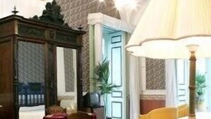 Um quarto com piso estampado, um armário de madeira, uma mesa com cadeiras, uma cama com cabeceira amarela e um abajur.