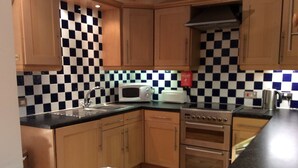 Uma cozinha com armários de madeira, bancada preta, micro-ondas, forno e painel de fundo xadrez.