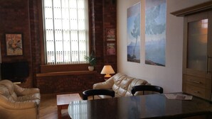 Uma sala de estar com sofá, mesa de jantar, televisão e janela com persianas.