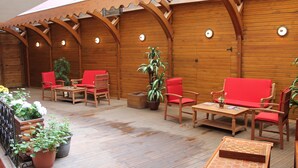 Um deck de madeira com cadeiras vermelhas e uma mesa, rodeado por vasos com plantas.