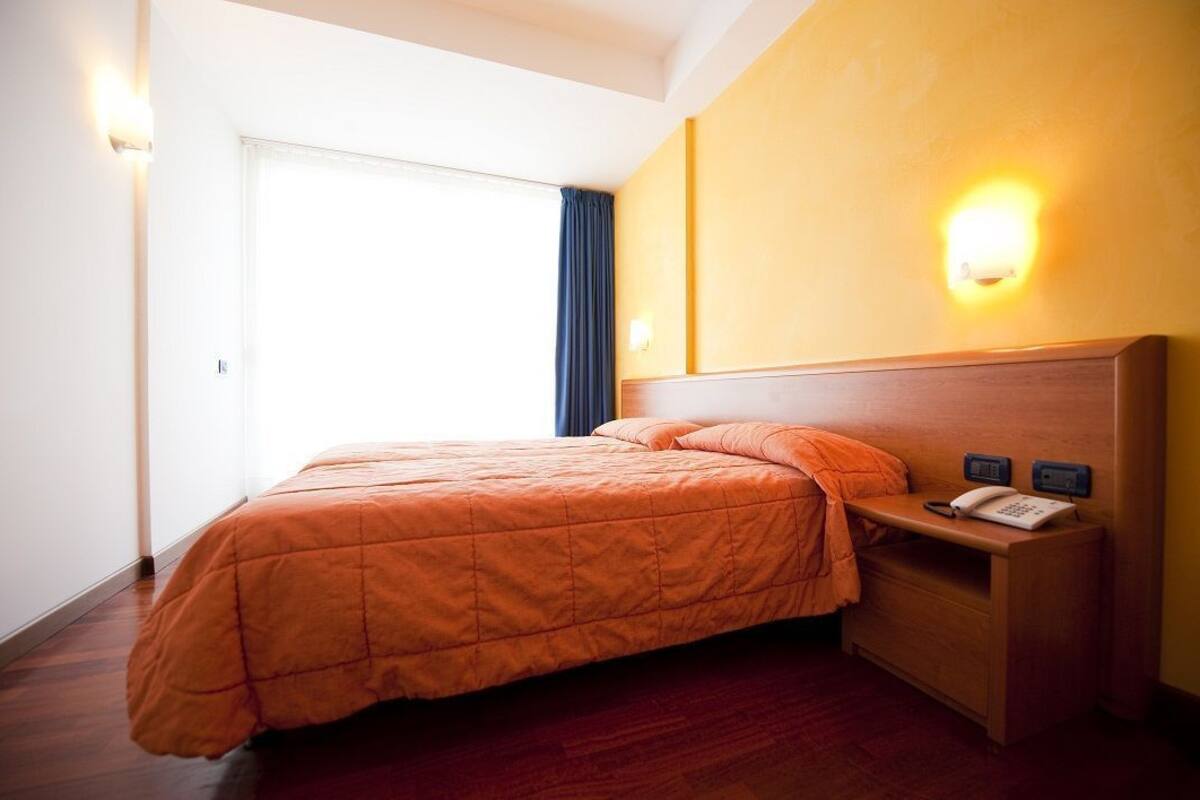 Quarto de hotel com cama, mesa de cabeceira e telefone fixado na parede.