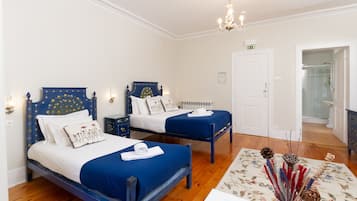 Quarto de hotel com duas camas, piso de madeira, um candelabro e um tapete floral.