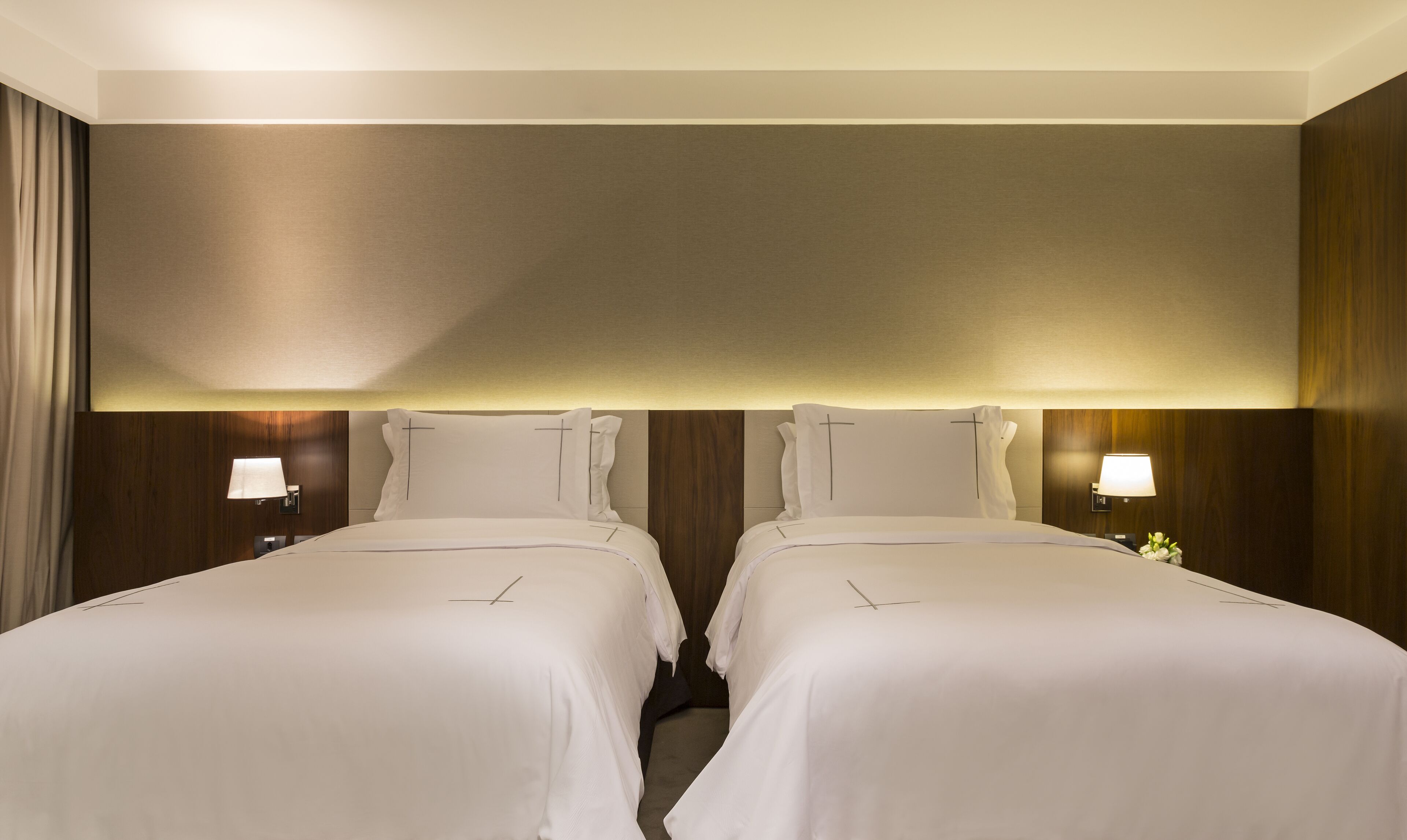 Quarto de hotel com duas camas, cabeceira de madeira e abajures.