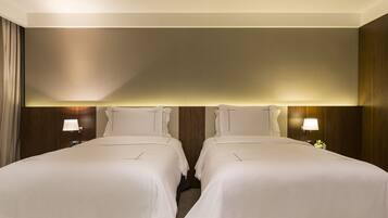 Quarto de hotel com duas camas, cabeceira de madeira e abajures.
