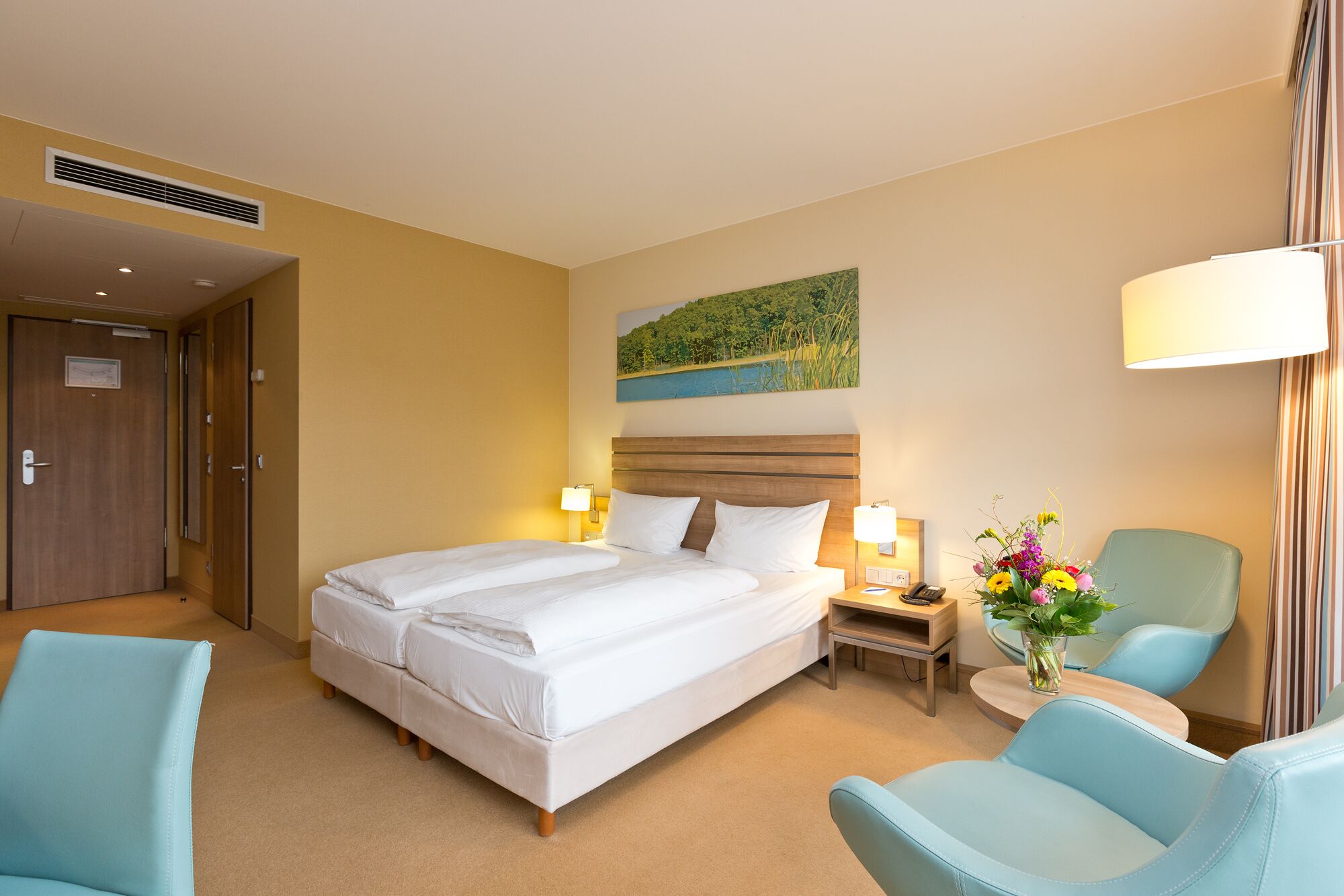 Quarto de hotel com uma cama grande, duas mesas de cabeceira com abajures, uma escrivaninha com cadeira e um quadro na parede.