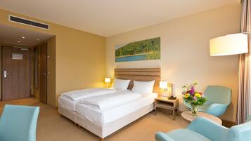 Quarto de hotel com uma cama grande, duas mesas de cabeceira com abajures, uma escrivaninha com cadeira e um quadro na parede.