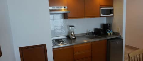 Cozinha compacta com armários de madeira, micro-ondas, cafeteira e geladeira.