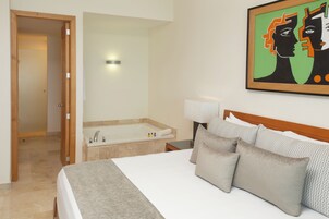 Quarto de hotel com uma cama, banheiro com banheira e um quadro na parede.