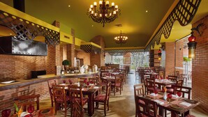 Restaurante com paredes de tijolo, mesas de madeira e cadeiras vermelhas acolchoadas.