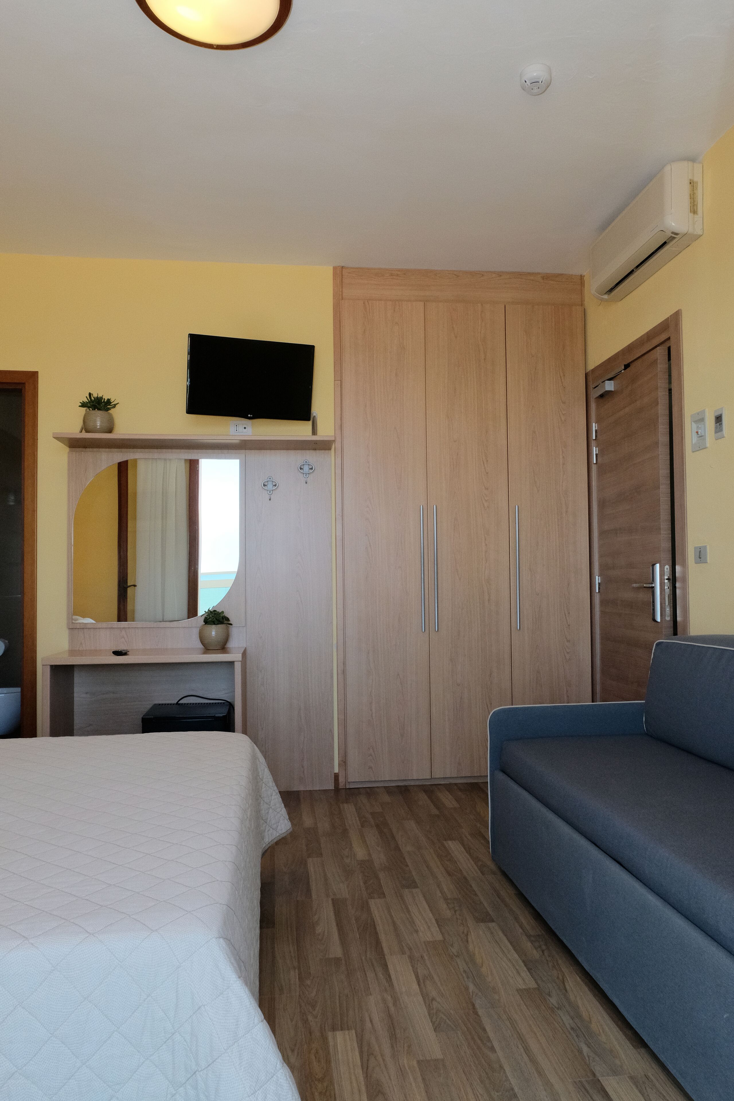 Quarto com cama, sofá, televisão, guarda-roupa e ar condicionado.