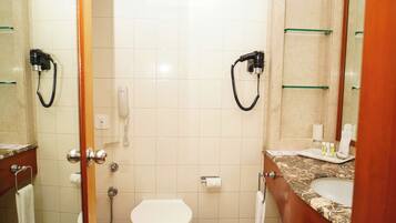 Casa de banho com sanita, lavatório e espelhos. Existem secadores de cabelo e um telefone na parede.