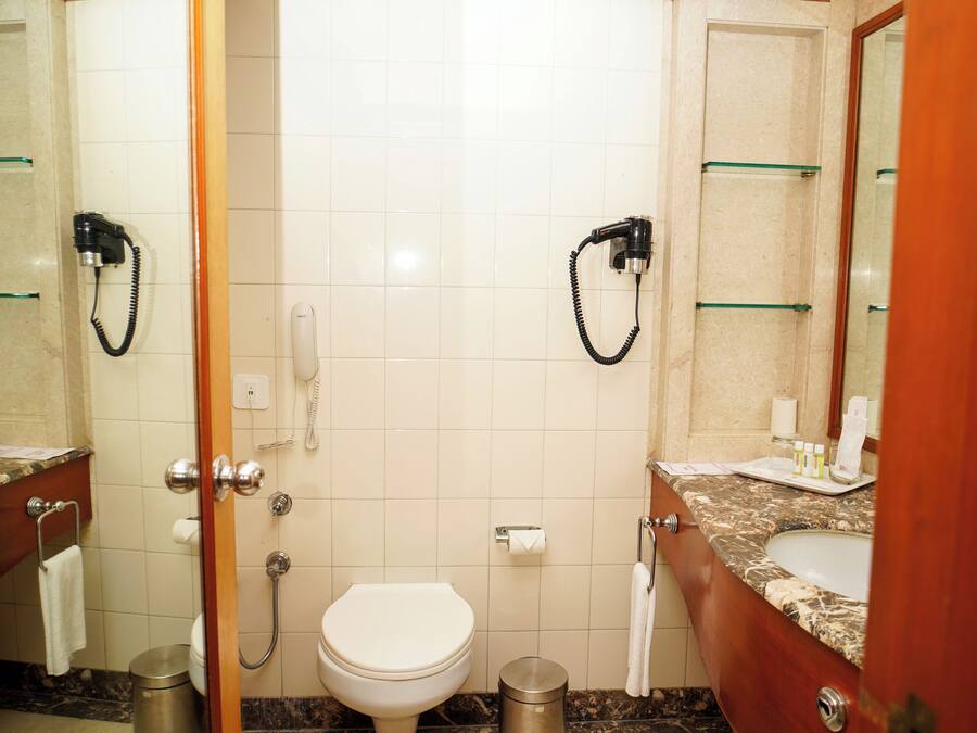 Casa de banho com sanita, lavatório e espelhos. Existem secadores de cabelo e um telefone na parede.