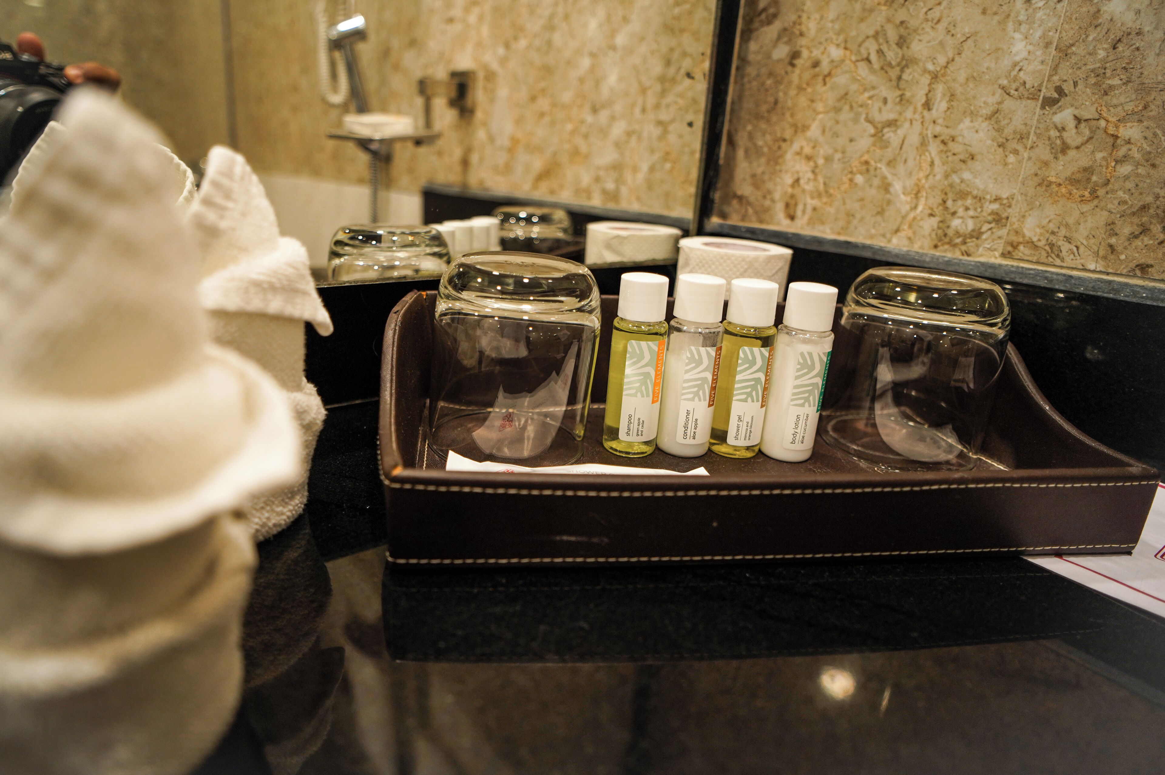 Uma bancada de banheiro com produtos de higiene pessoal, incluindo uma toalha, um pote de vidro e várias embalagens de loção.