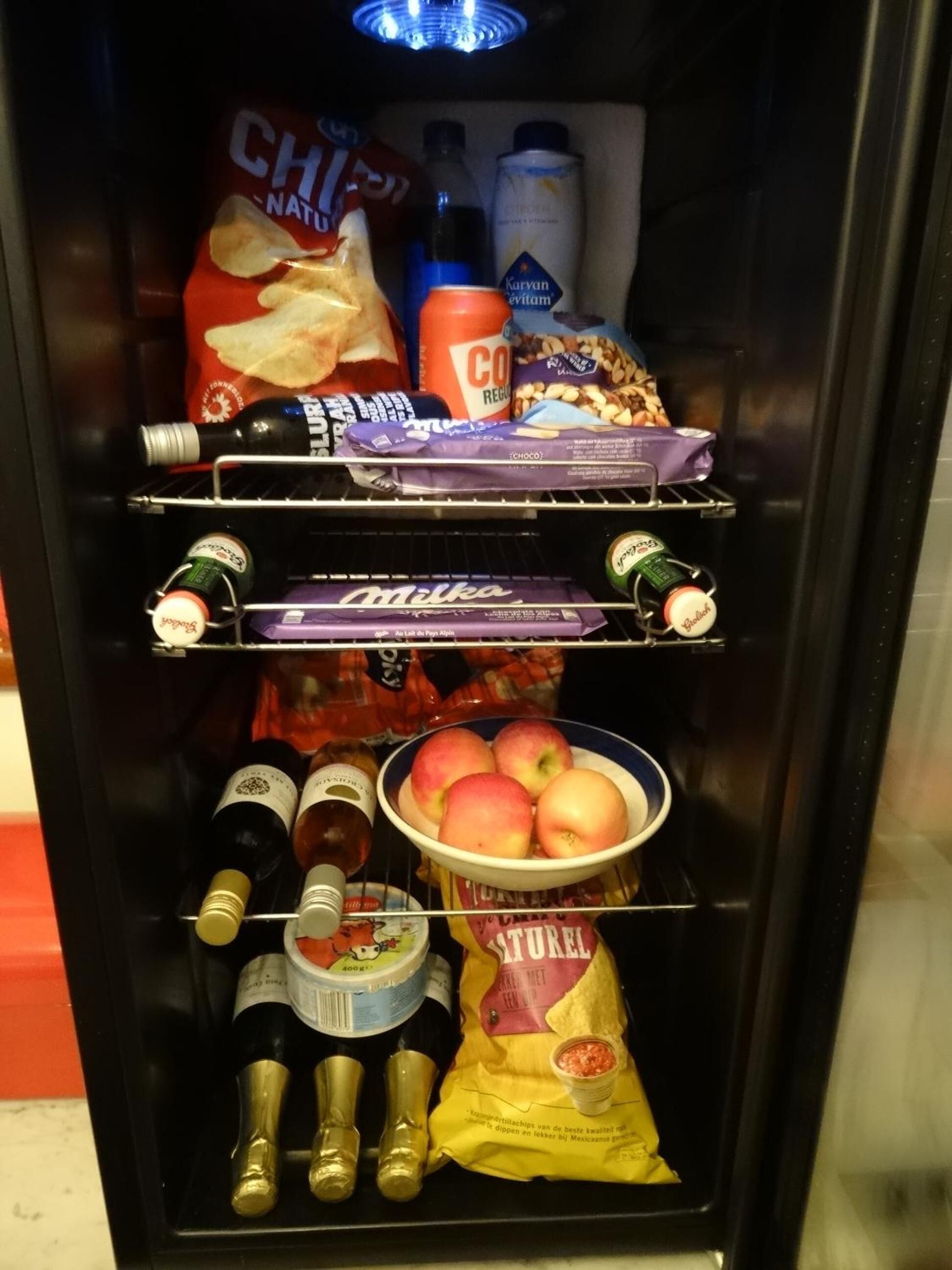 Um minibar com lanches, bebidas e uma taça de maçãs.