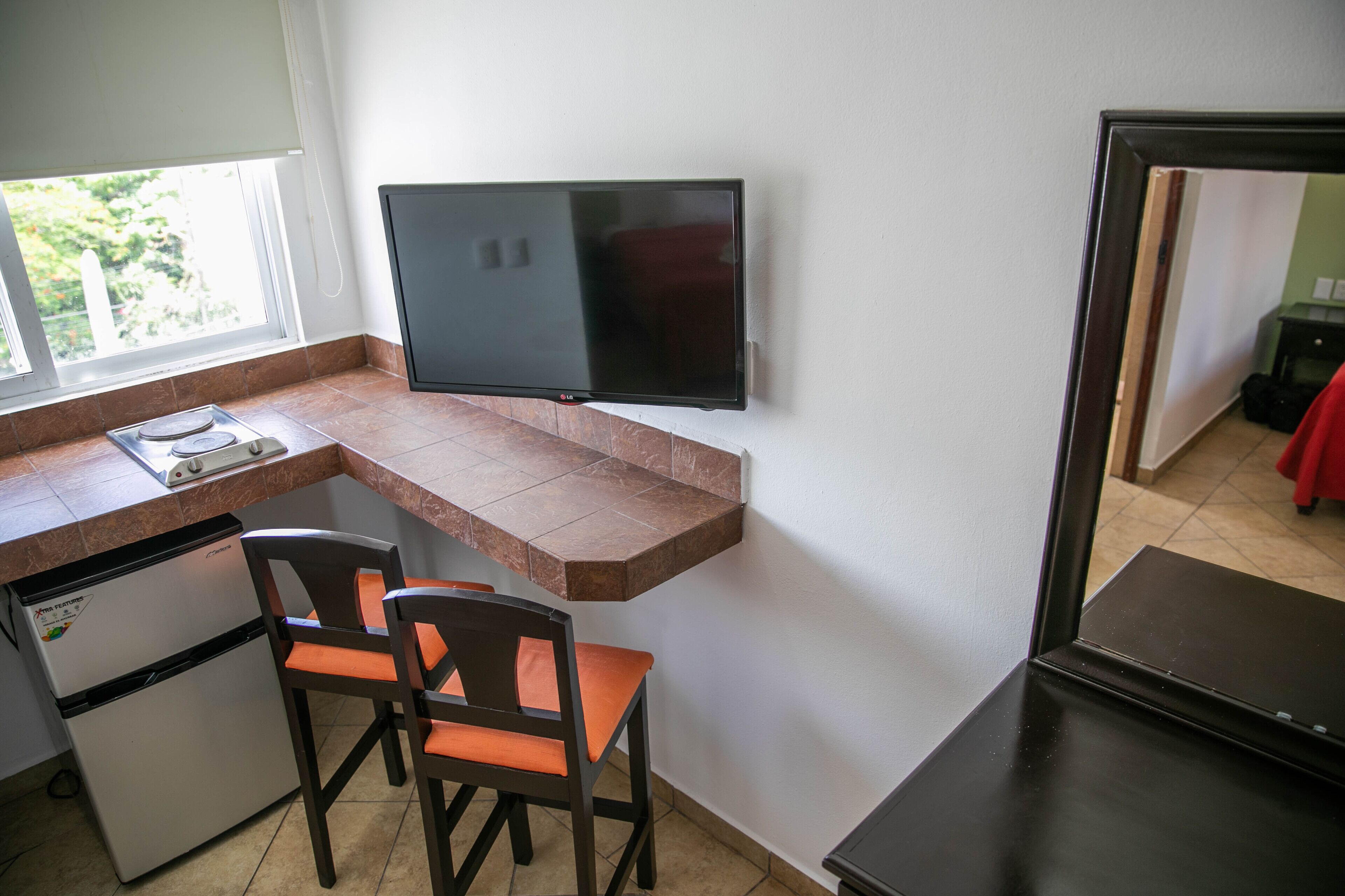 Cozinha compacta com televisão integrada, um frigorífico pequeno e duas cadeiras.