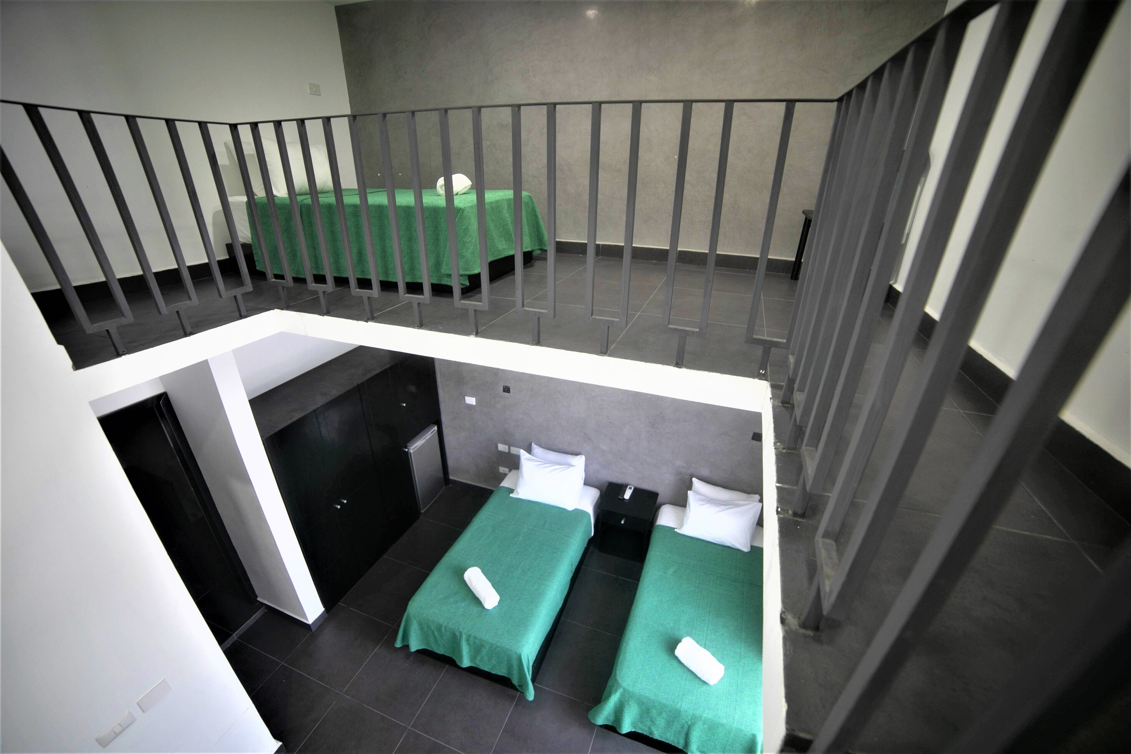Quarto de hotel com duas camas de solteiro, uma secretária pequena e um edredom verde.