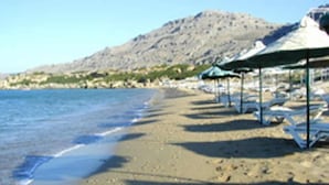 Uma praia com guarda-sóis e espreguiçadeiras, uma montanha ao fundo e um céu claro.