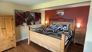 Quarto com cama de madeira, duas mesas de cabeceira, um criado-mudo e um guarda-roupa, além de duas luminárias fixadas na parede.