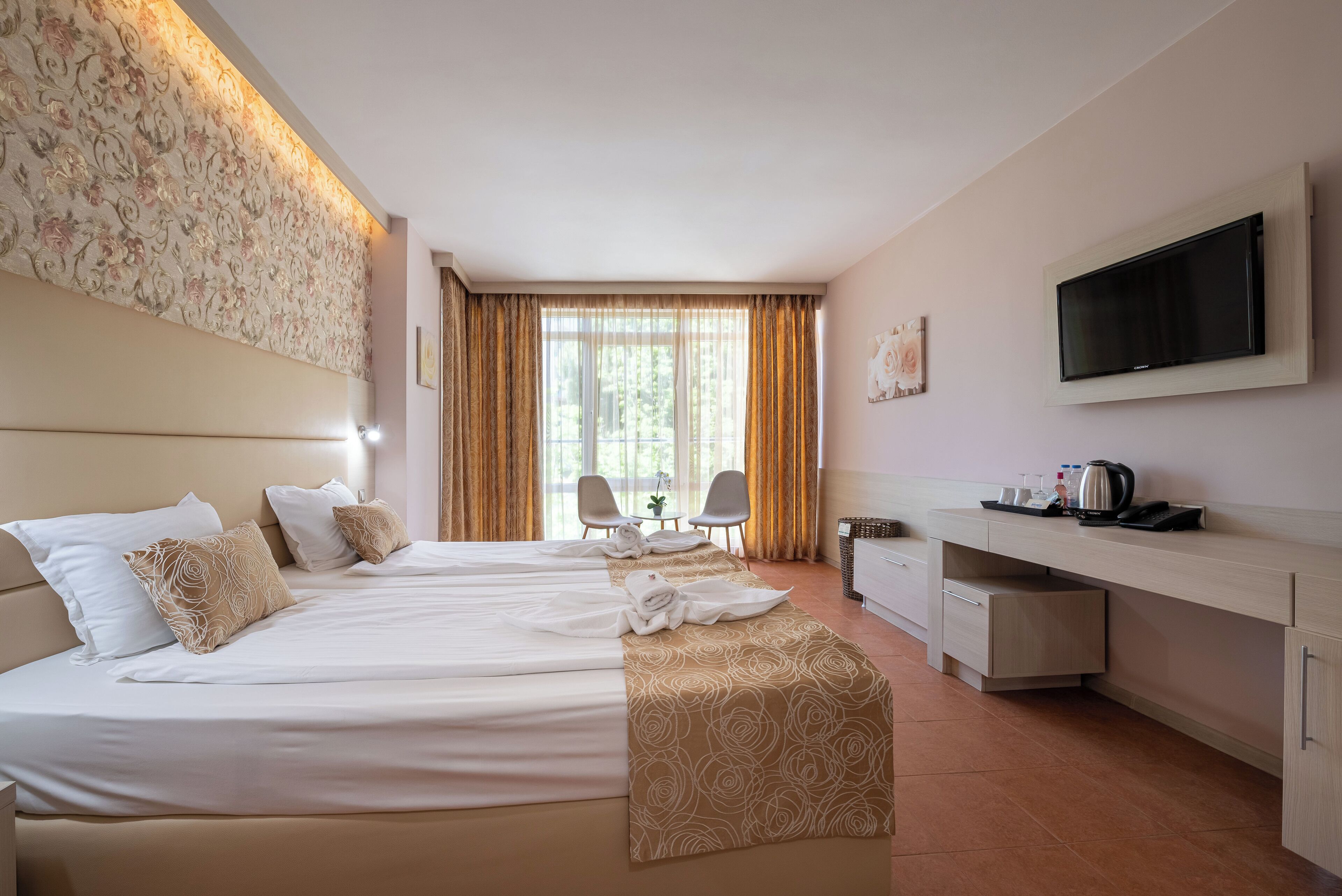 Quarto de hotel com cama grande, escrivaninha, televisão e janela com cortinas.
