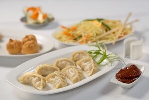 Uma mesa com diversos pratos, incluindo dumplings, um prato de macarrão e uma pequena tigela de molho.