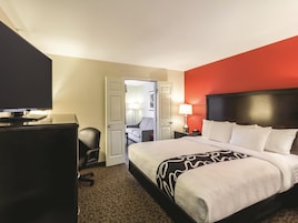 Quarto de hotel com cama, escrivaninha, cadeira e televisão.