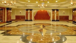 Um hall amplo com um grande e elaborado desenho de carpete, um palco central e luminárias elegantes.