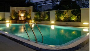 Piscina com escadas de metal, rodeada por paredes com plantas e um candeeiro decorativo fixado na parede.