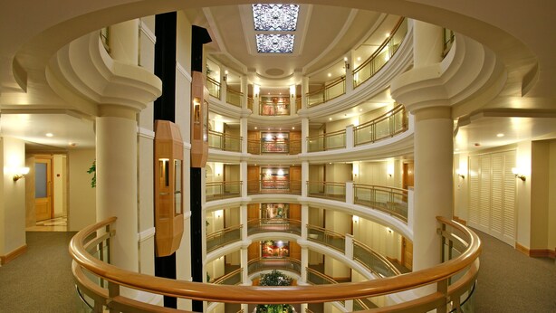 Um átrio com vários níveis, jardim central, grades de vidro e design arquitetônico moderno.
