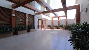 Um espaço amplo e interno com piso de azulejos, vigas de madeira e plantas em vasos.