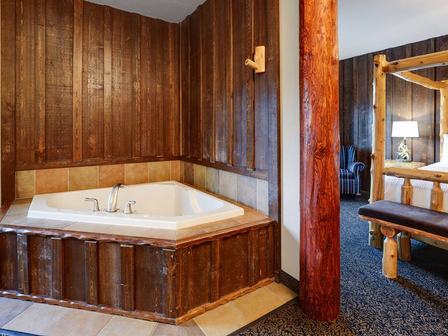 Um banheiro em estilo cabana de madeira, com uma banheira livre, um banco de madeira e uma cabeceira de madeira.