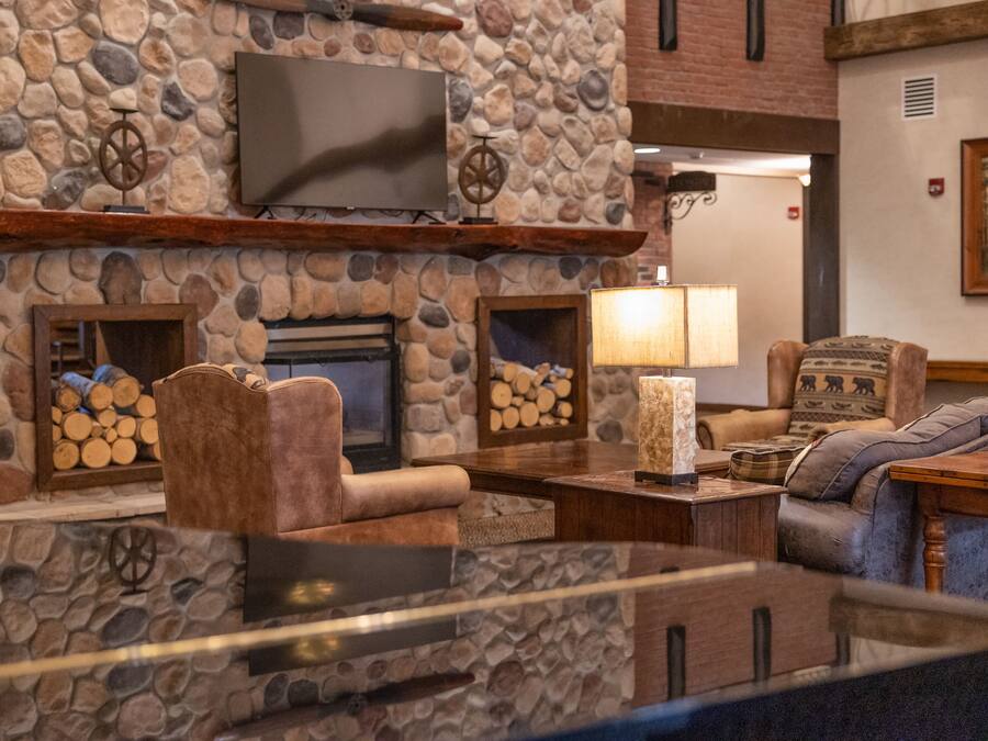 Uma lareira de pedra com televisão na parede, uma mesa de madeira e um sofá num ambiente acolhedor.