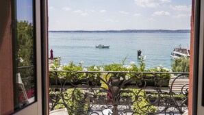 Vista de uma varanda com vista para águas calmas, barcos, uma linha de costa distante e céu claro.