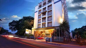 Um hotel de vários andares com entrada destacada, varandas e uma bandeira no topo.