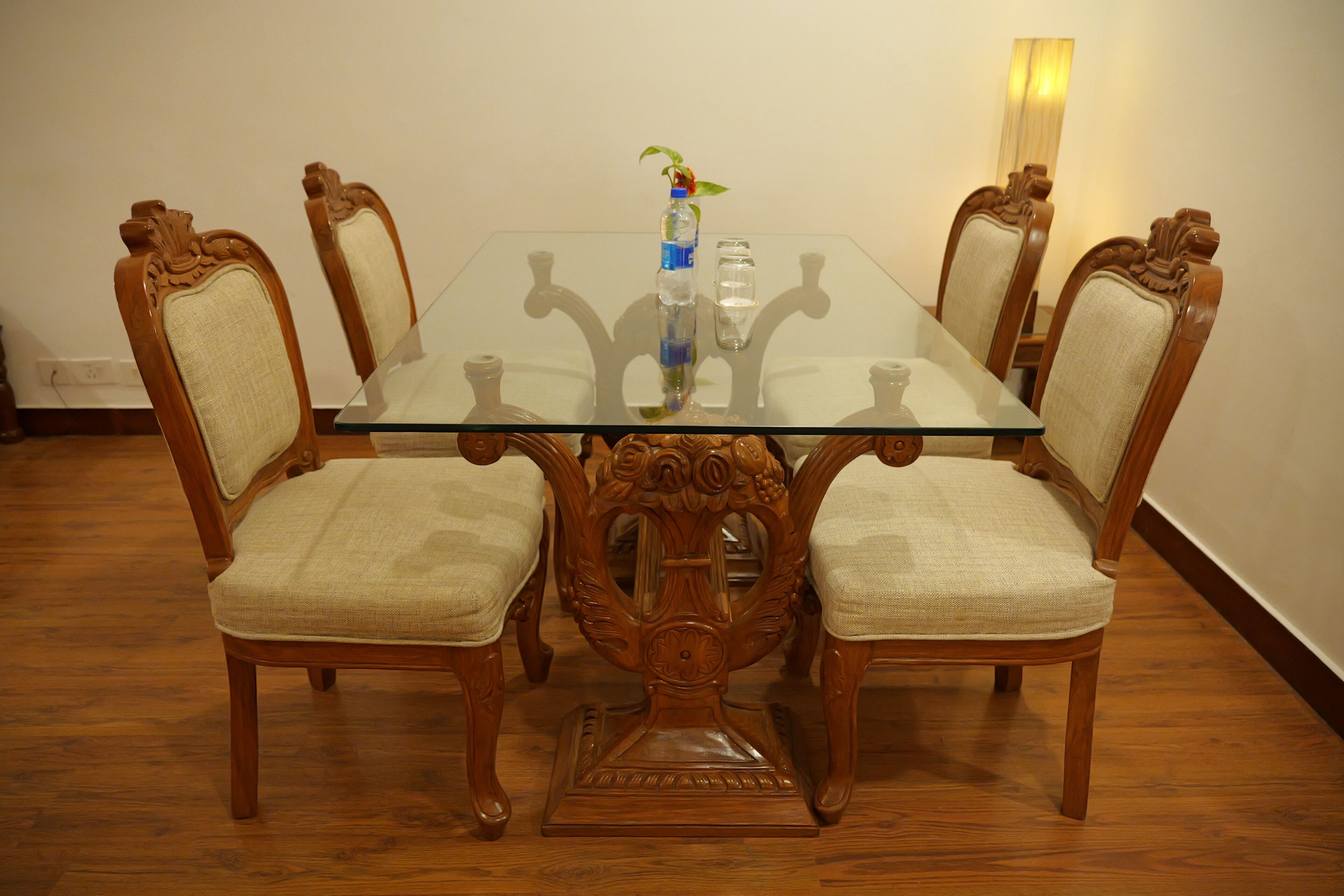 Uma mesa de jantar com tampo de vidro e cadeiras de madeira, uma garrafa e um copo sobre a mesa.