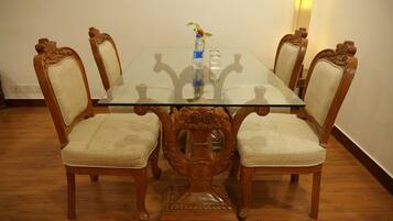 Uma mesa de jantar com tampo de vidro e cadeiras de madeira, uma garrafa e um copo sobre a mesa.