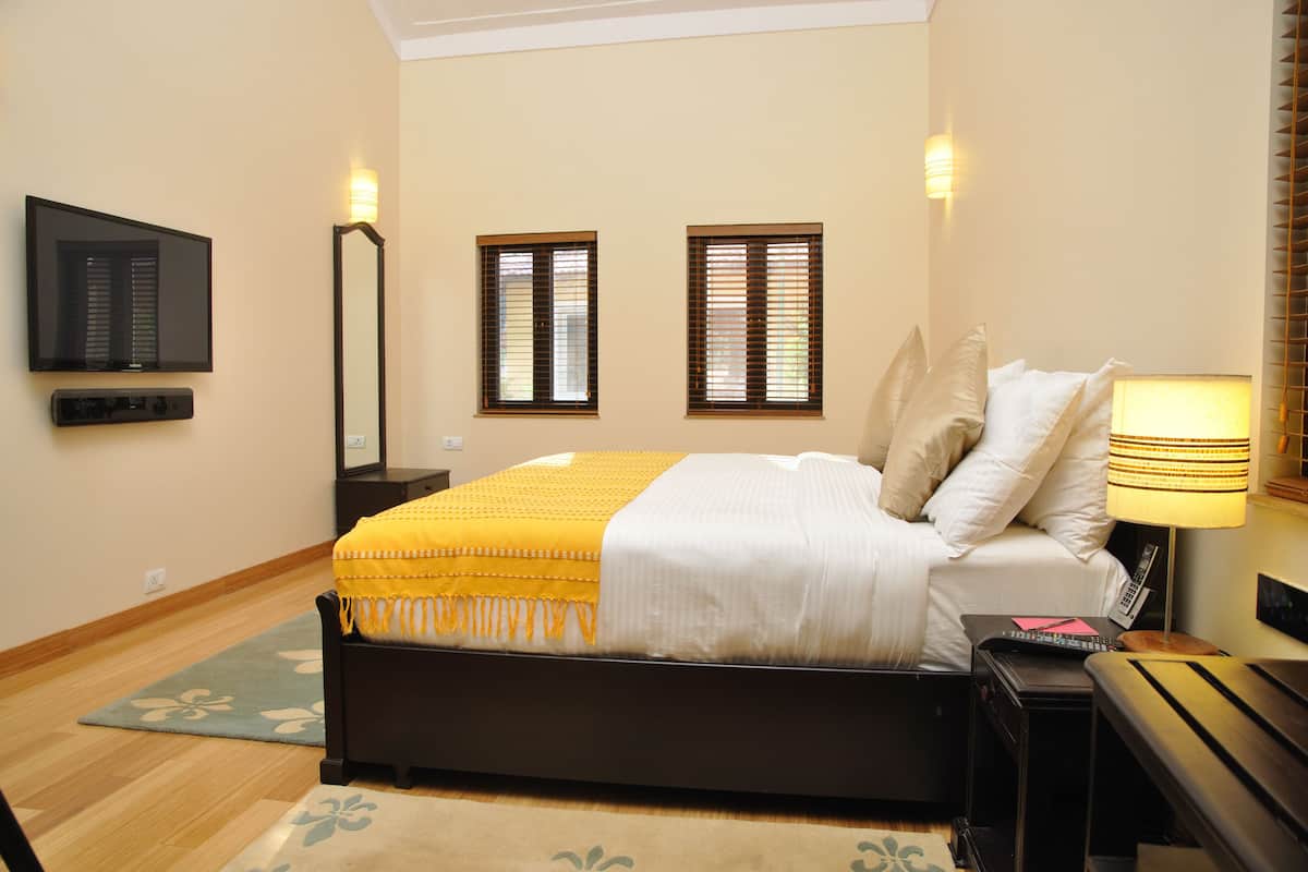 Quarto com cama, mesas de cabeceira, televisão e janelas com persianas.