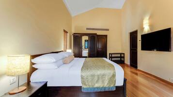 Quarto de hotel com cama, luminária de cabeceira, televisão, guarda-roupa e espelho.