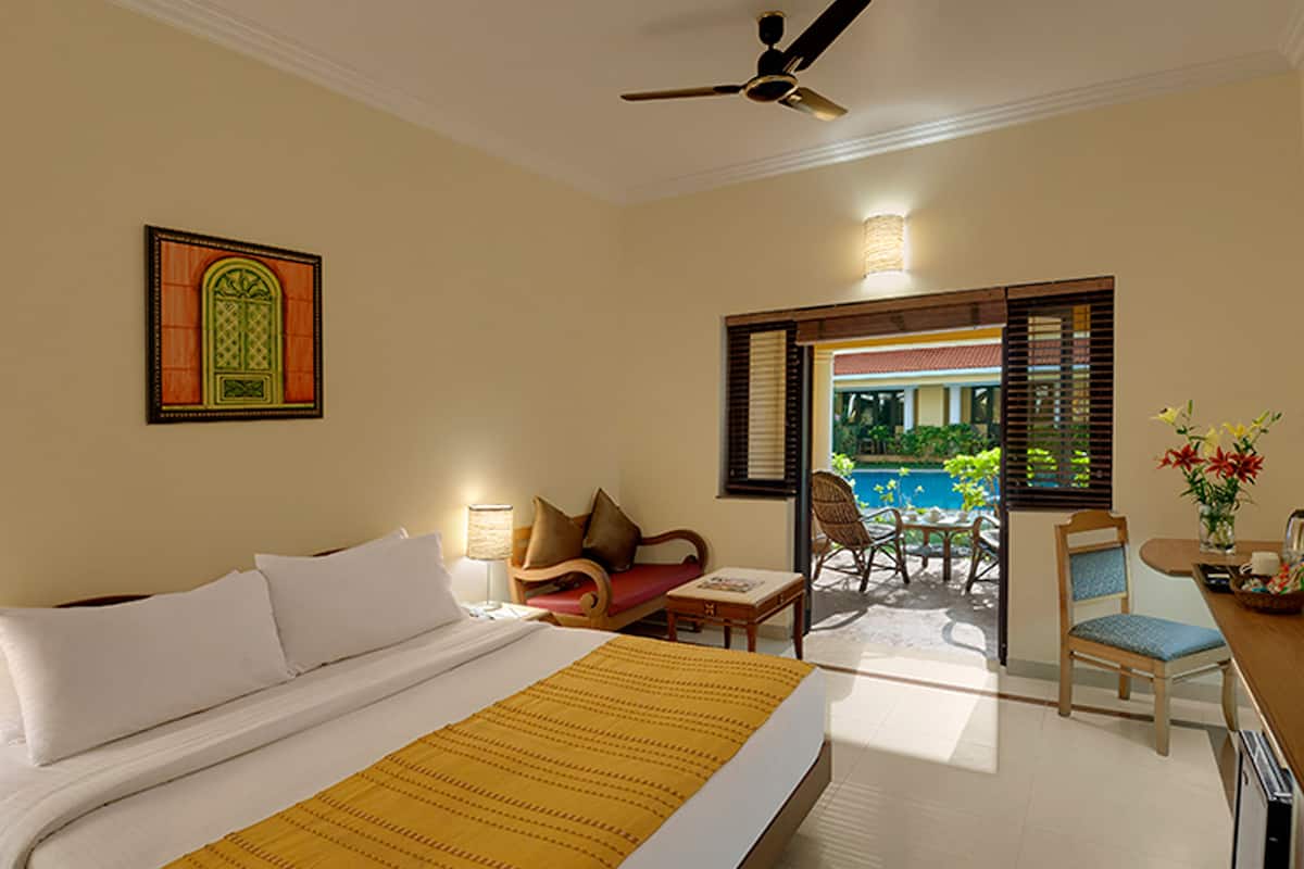 Quarto de hotel com cama, escrivaninha, cadeira, mesa, ventilador de teto e vista para a piscina.