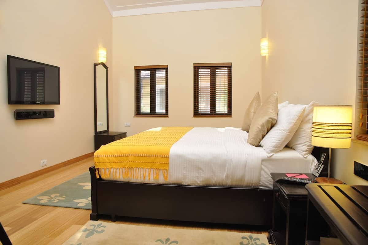 Quarto com cama, mesas de cabeceira, televisão e duas janelas com persianas.