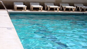 Piscina com água cristalina, cercada por cadeiras de descanso brancas.