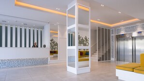 Um lobby moderno com uma mesa de recepção, um sofá amarelo, uma escada e um elevador.